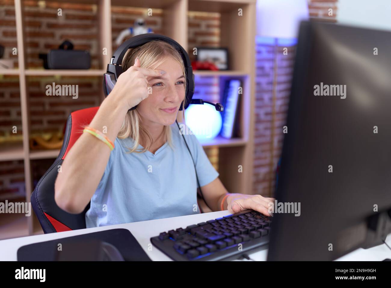 Young caucasian woman playing video games wearing headphones pointing ...