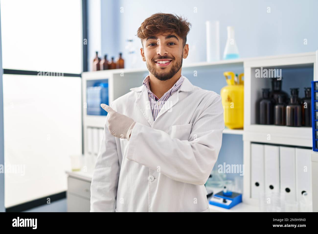 Arab man with beard working at scientist laboratory smiling cheerful pointing with hand and ...