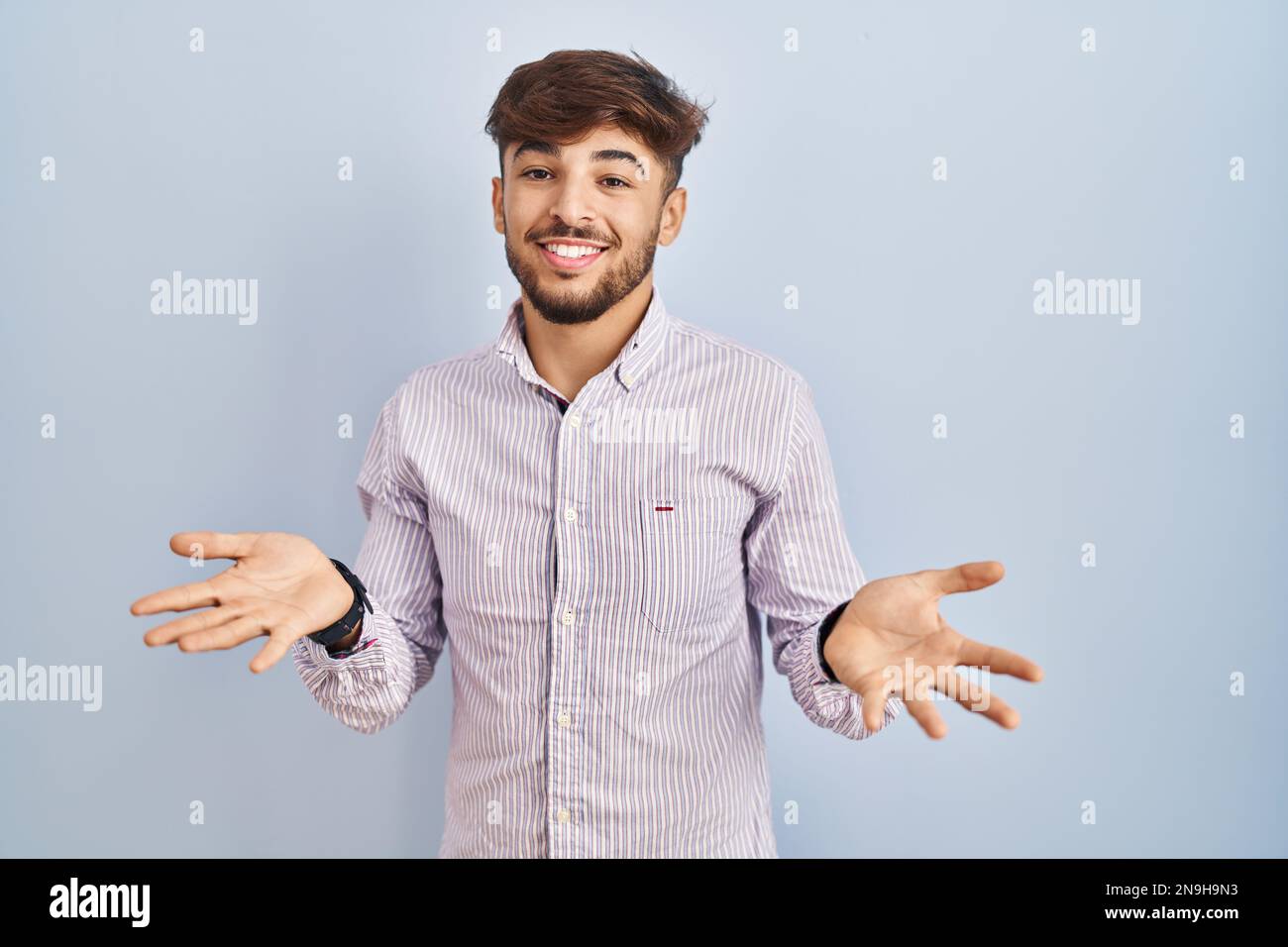 Arab man with beard standing over blue background smiling cheerful ...
