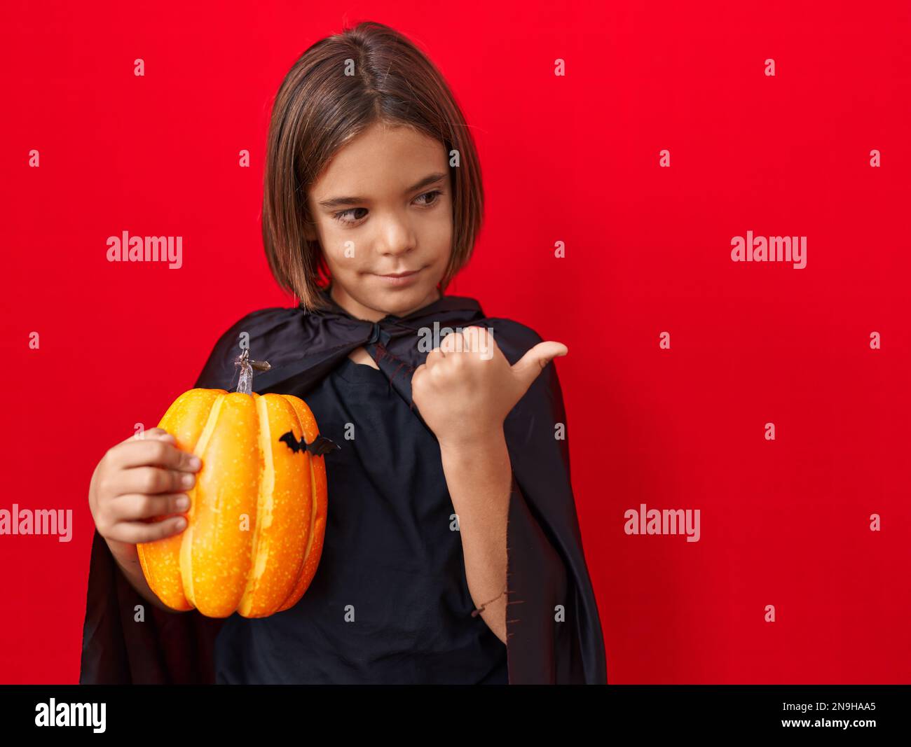 Little hispanic boy wearing a cape and holding halloween pumpkin doing ...