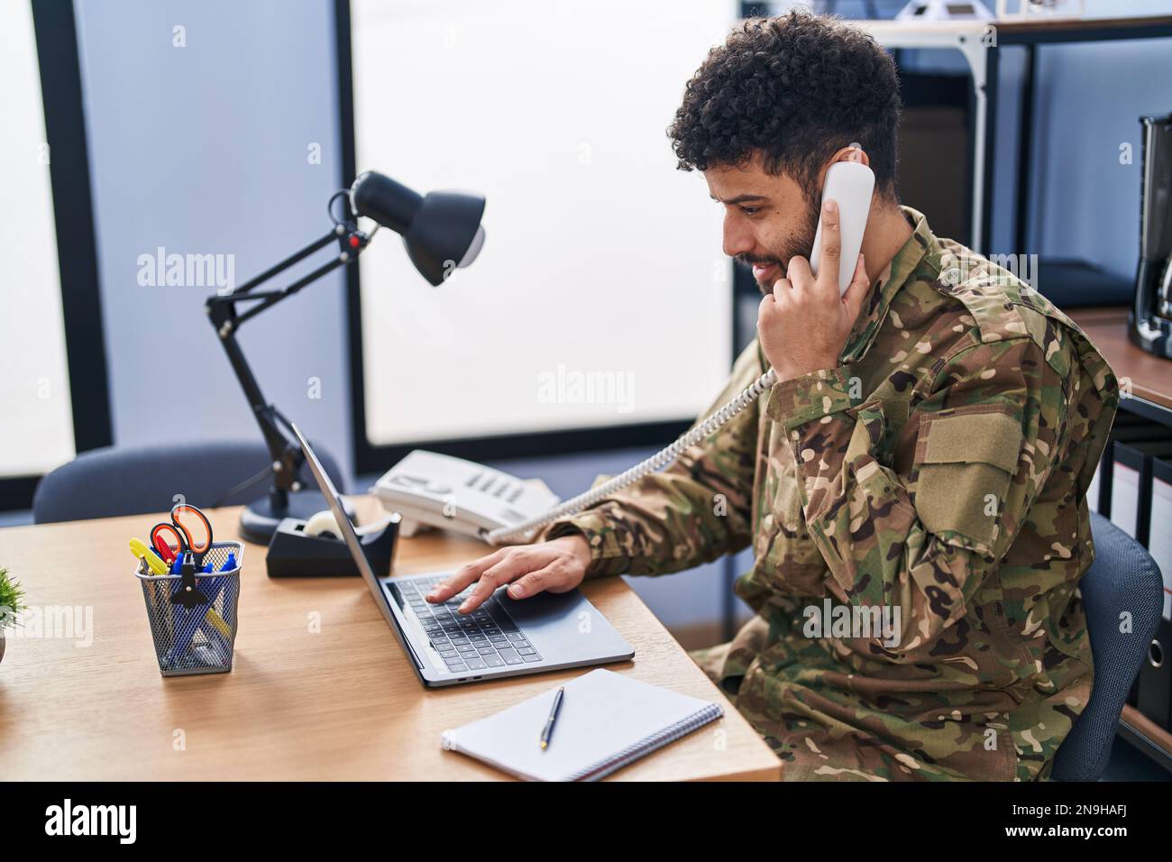 Young arab man army soldier using laptop talking on the telephone at ...