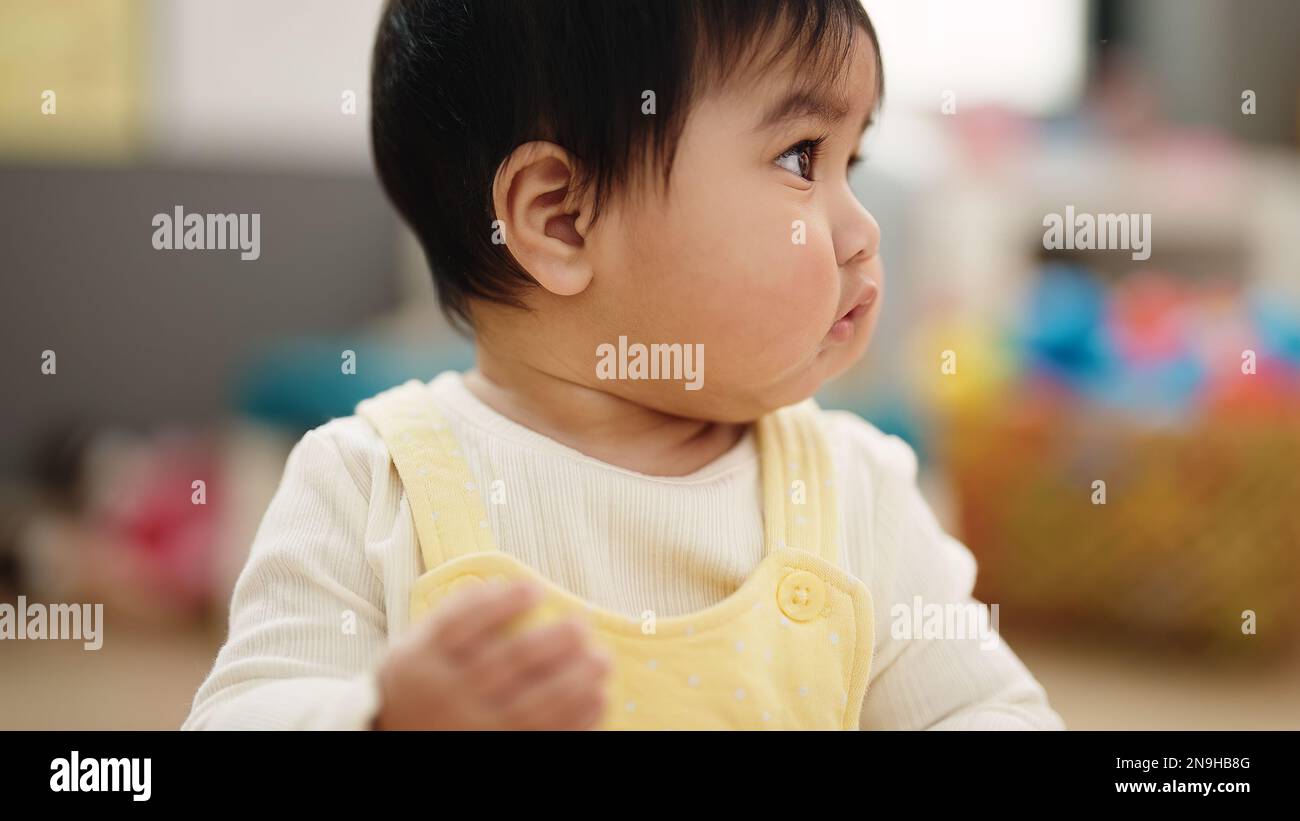 Adorable hispanic baby sitting on floor with relaxed expression at ...