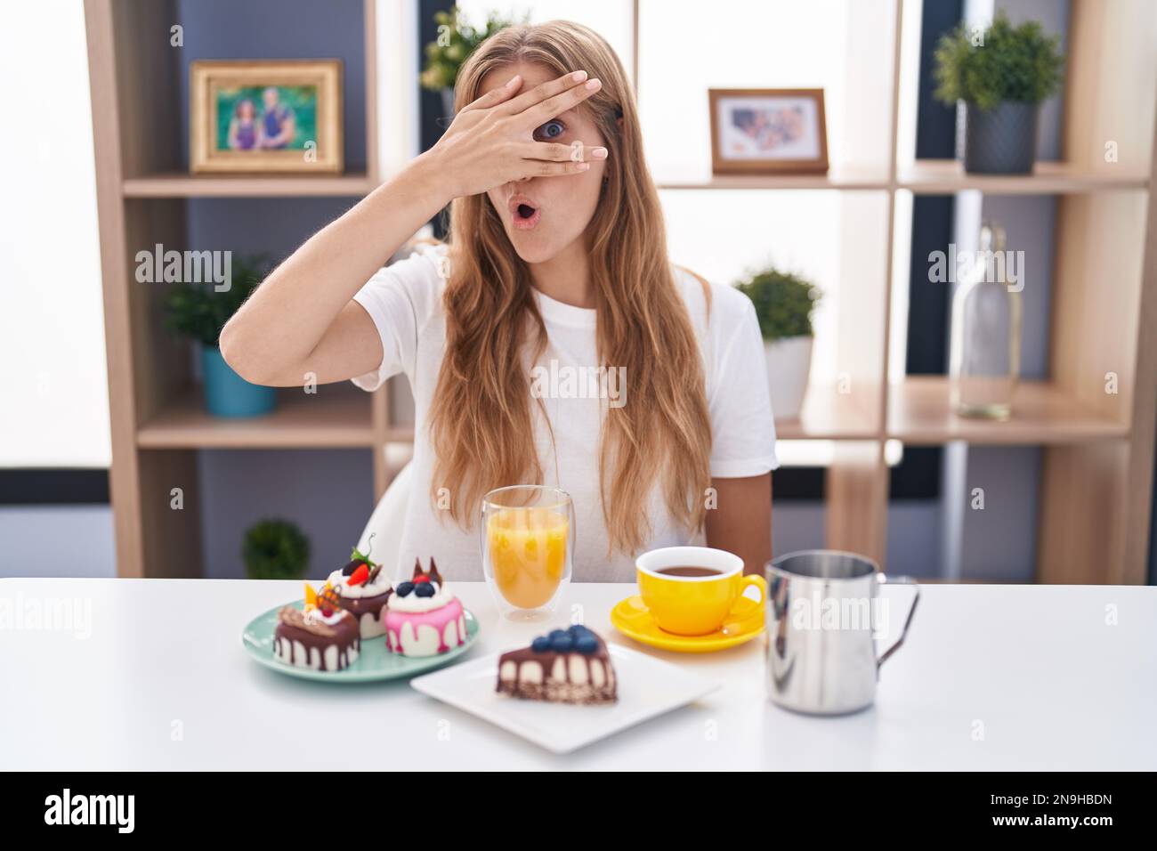 Young caucasian woman eating pastries t for breakfast peeking in shock ...