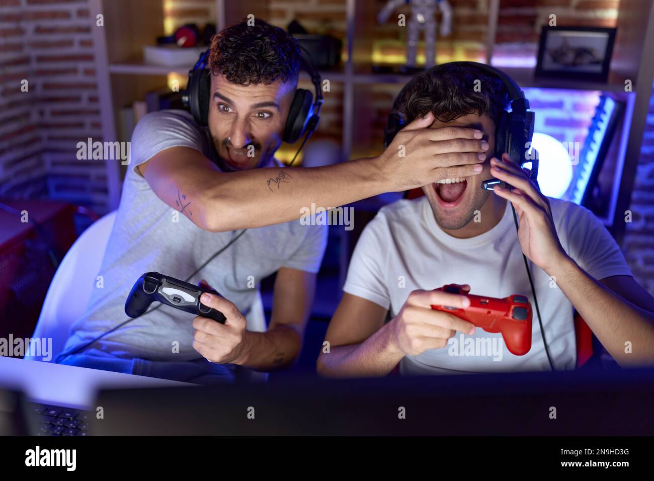Two hispanic men streamers playing video game covering eyes cheating at ...