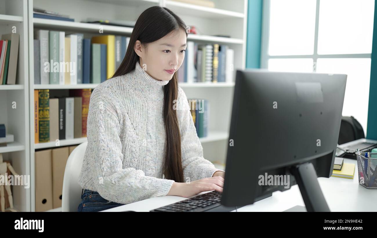 Young chinese woman student using computer studying at library ...