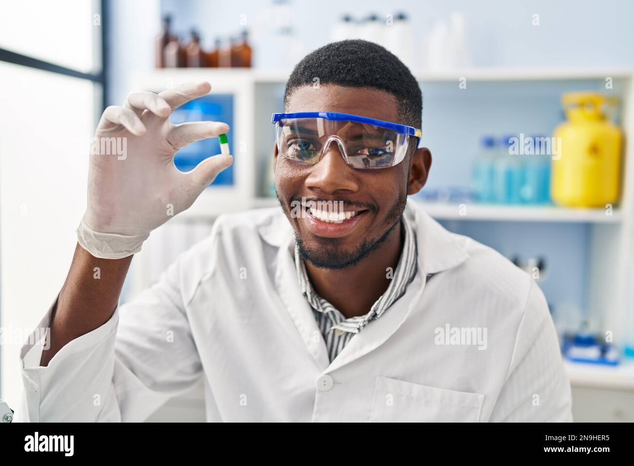 Young african american man wearing scientist uniform holding pill at ...