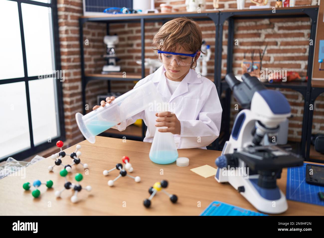 Adorable caucasian boy student pouring liquid on test tube at classroom ...
