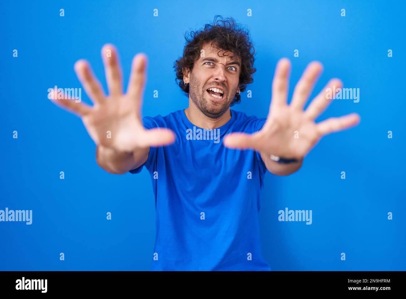 Hispanic young man standing over blue background afraid and terrified ...
