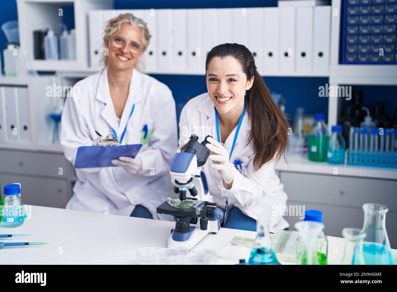 Two women scientists using microscope write on document at laboratory ...