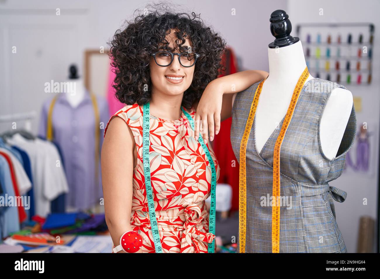 Young middle eastern woman tailor smiling confident leaning on manikin ...