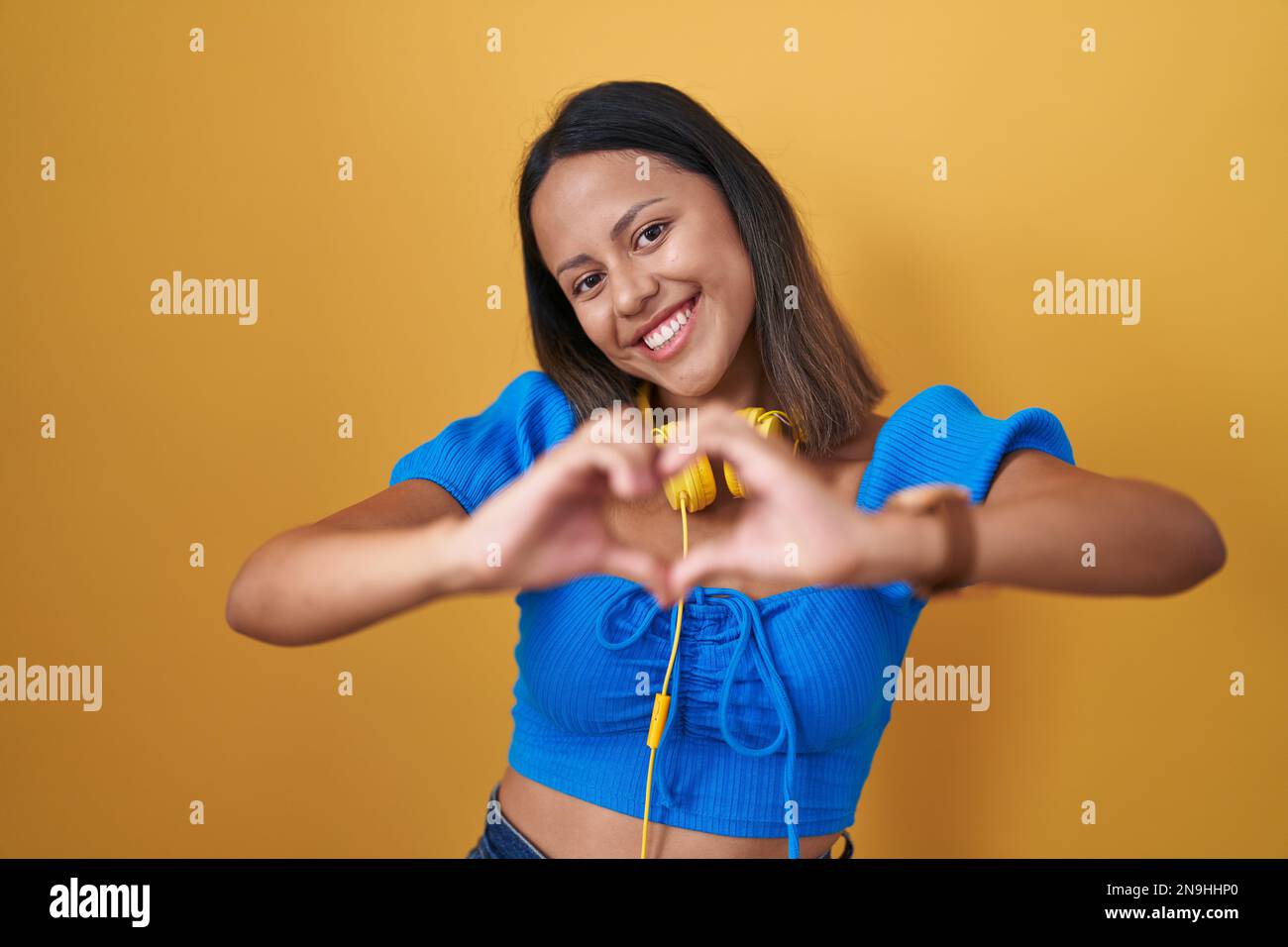 Hispanic young woman standing over yellow background smiling in love ...