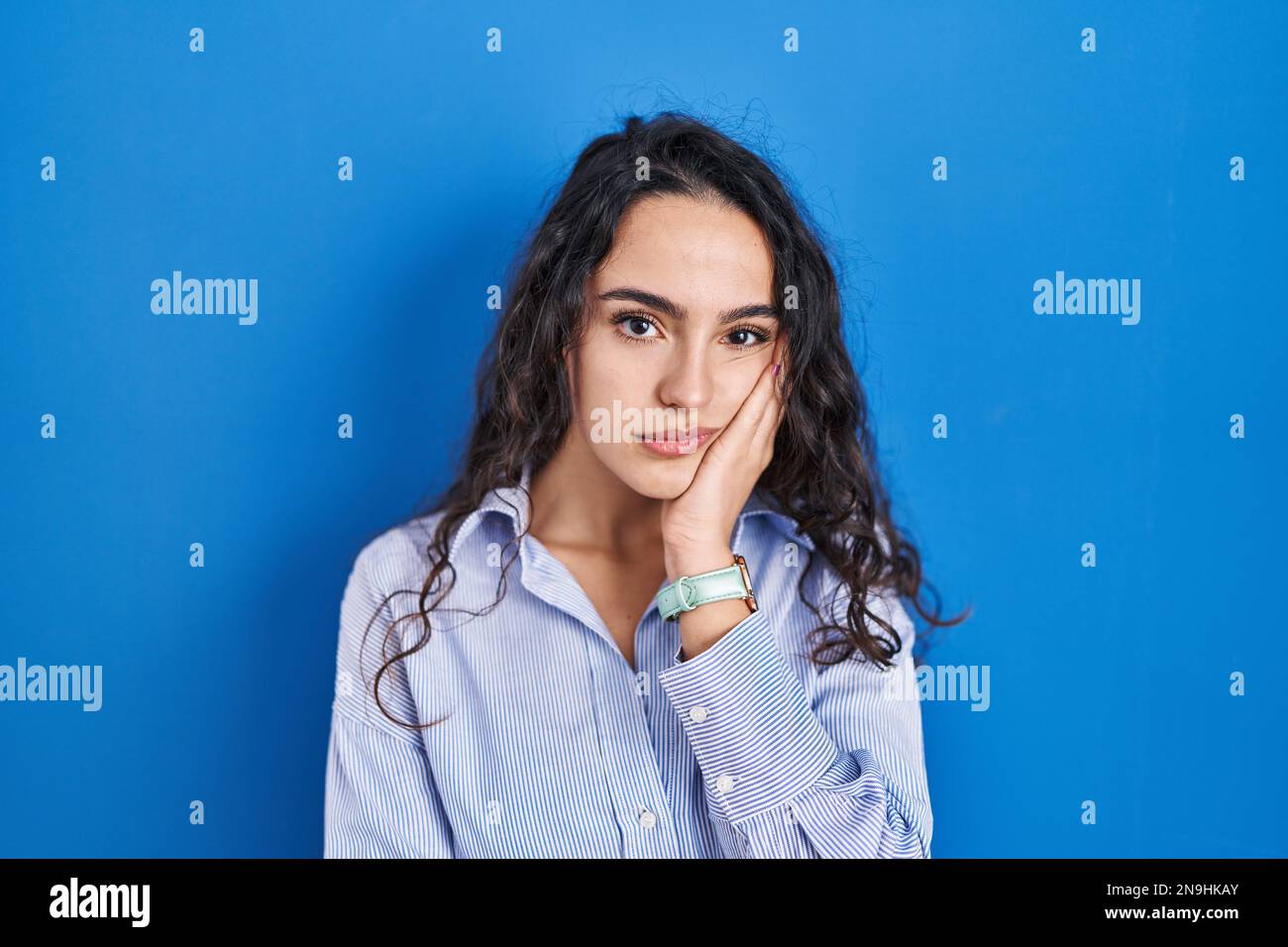 Young brunette woman standing over blue background thinking looking ...