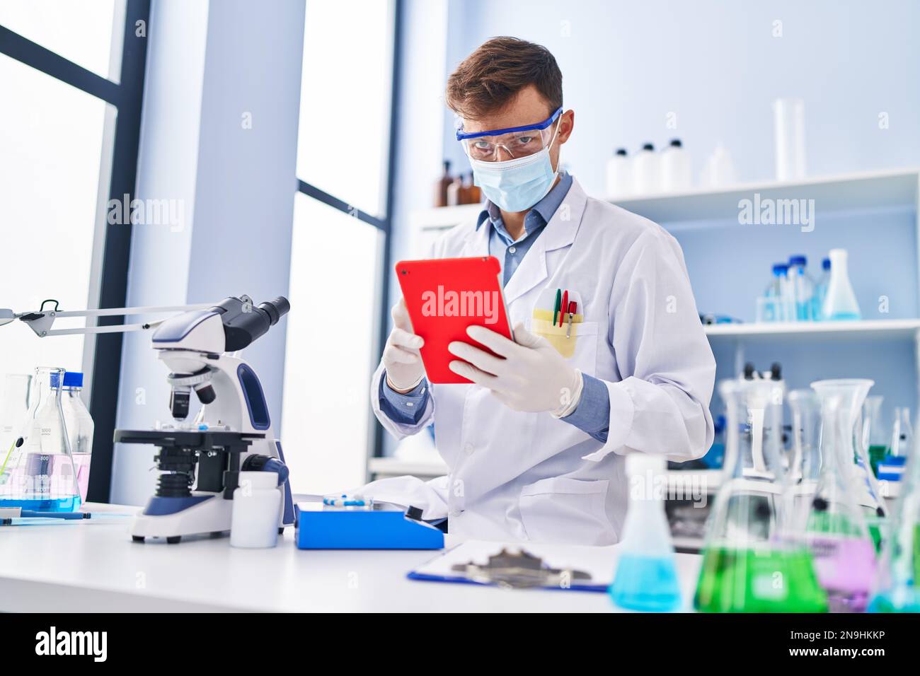 Young man scientist wearing medical mask using touchpad at laboratory ...