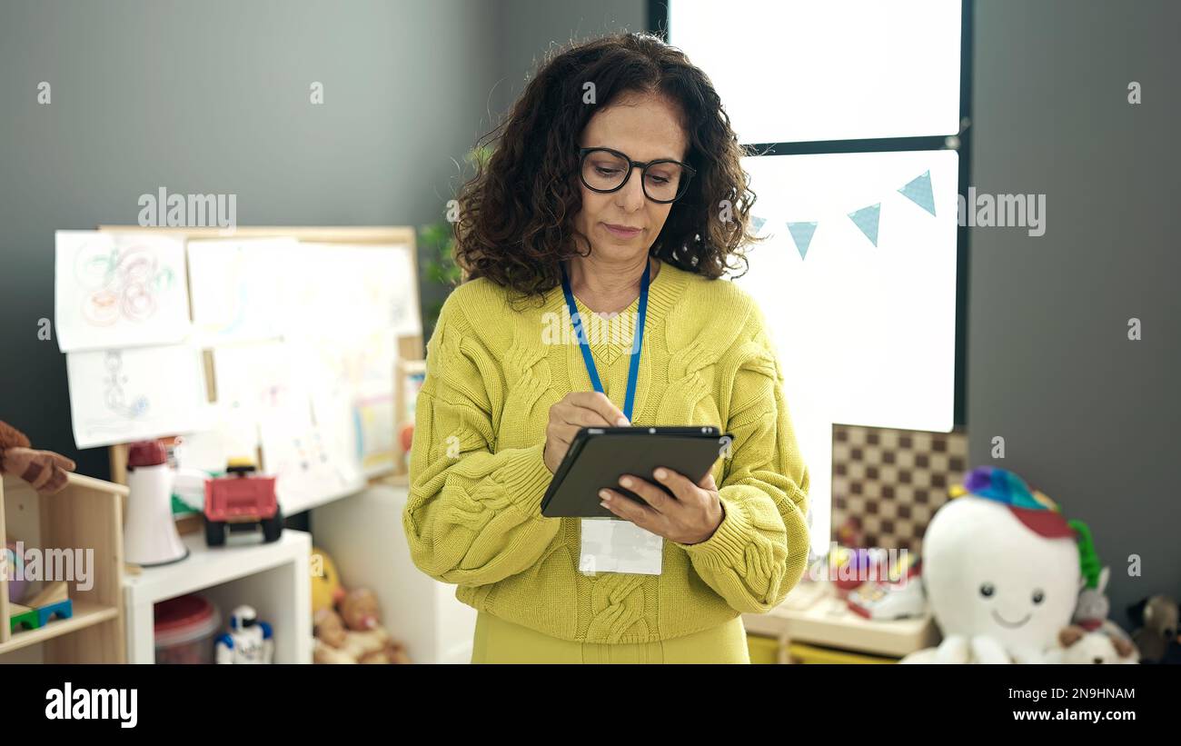 Middle age hispanic woman preschool teacher using touchpad at ...