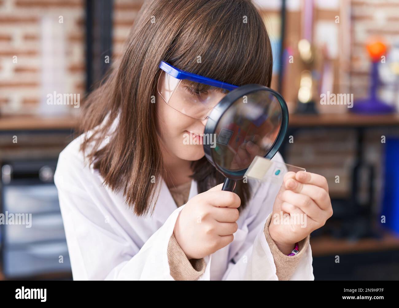 Adorable hispanic girl student looking sample using magnifying glass at ...
