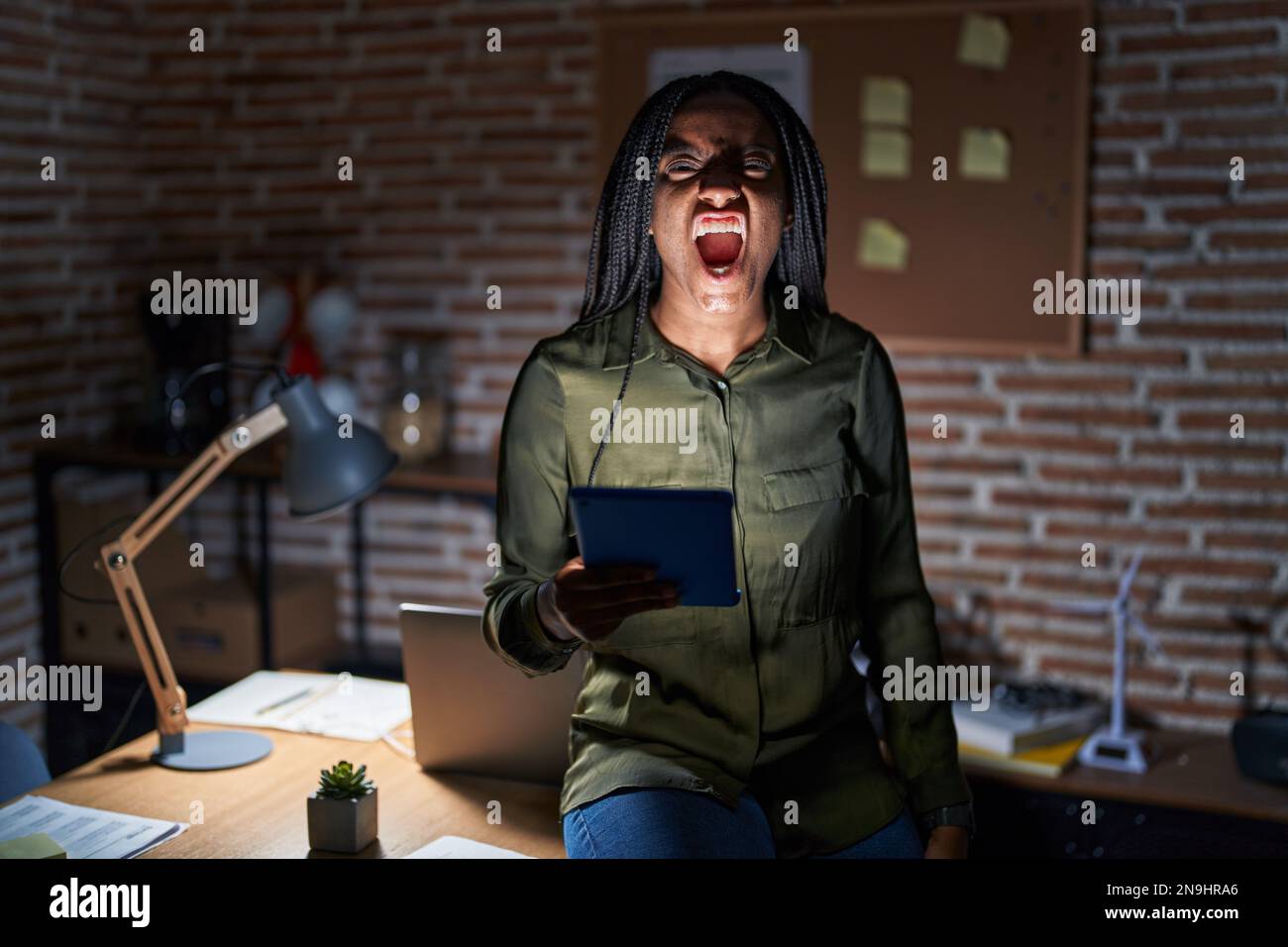 Young african american with braids working at the office at night angry ...