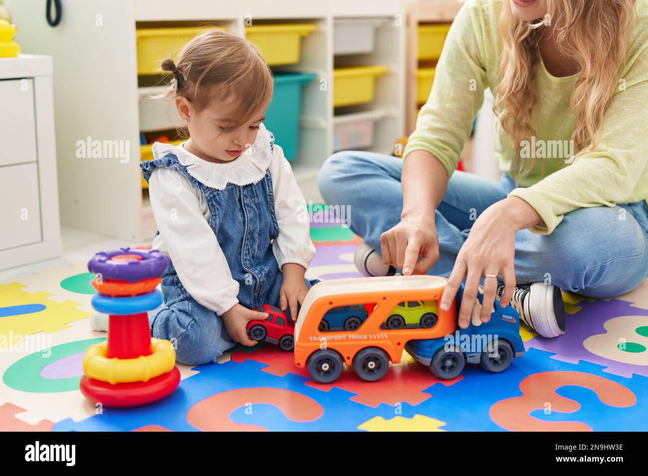 Teacher and toddler playing with cars toy sitting on floor at ...