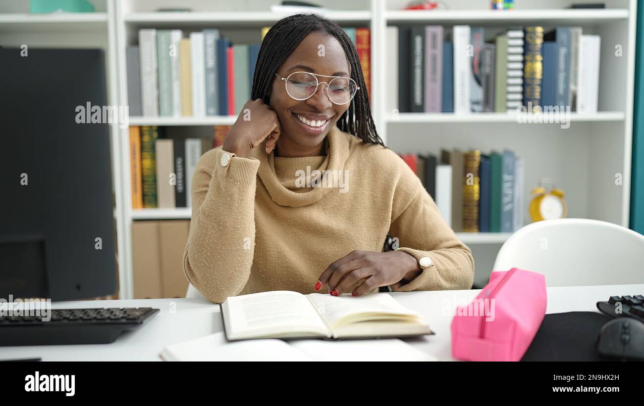 African woman reading a book sitting on desk at library university ...