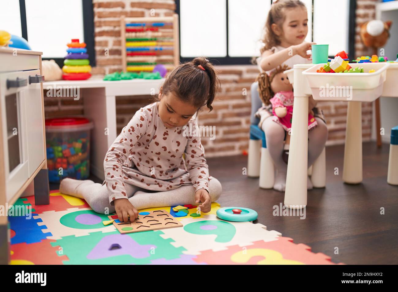Two kids playing with maths puzzle game and doll sitting on floor at ...