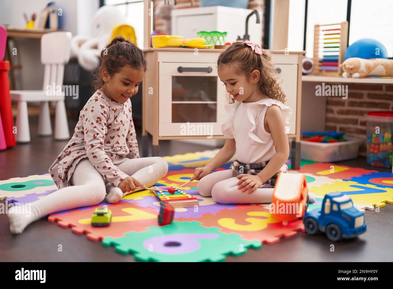 Two kids playing xylophone sitting on floor at kindergarten Stock Photo ...