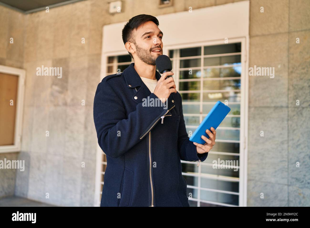 Young hispanic man reporter working using microphone and touchpad at ...