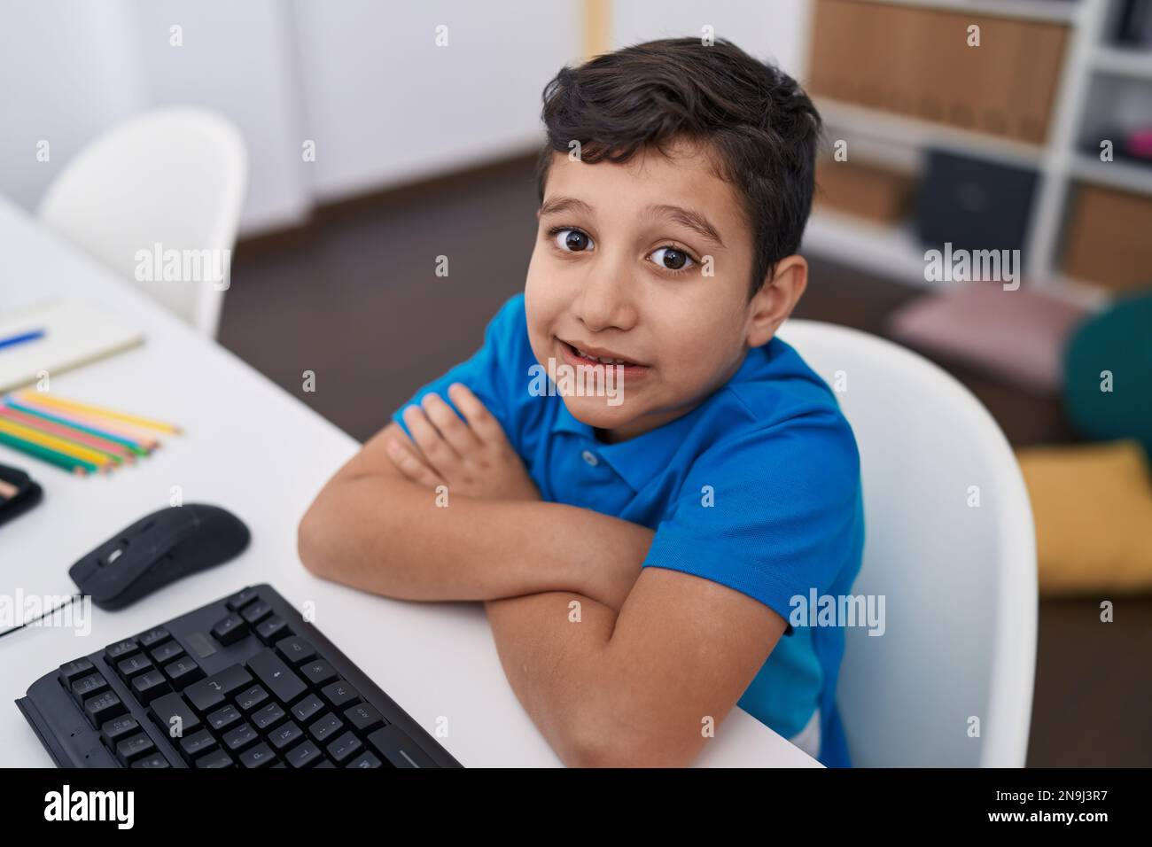 Adorable hispanic boy student using computer sitting on table with arms ...