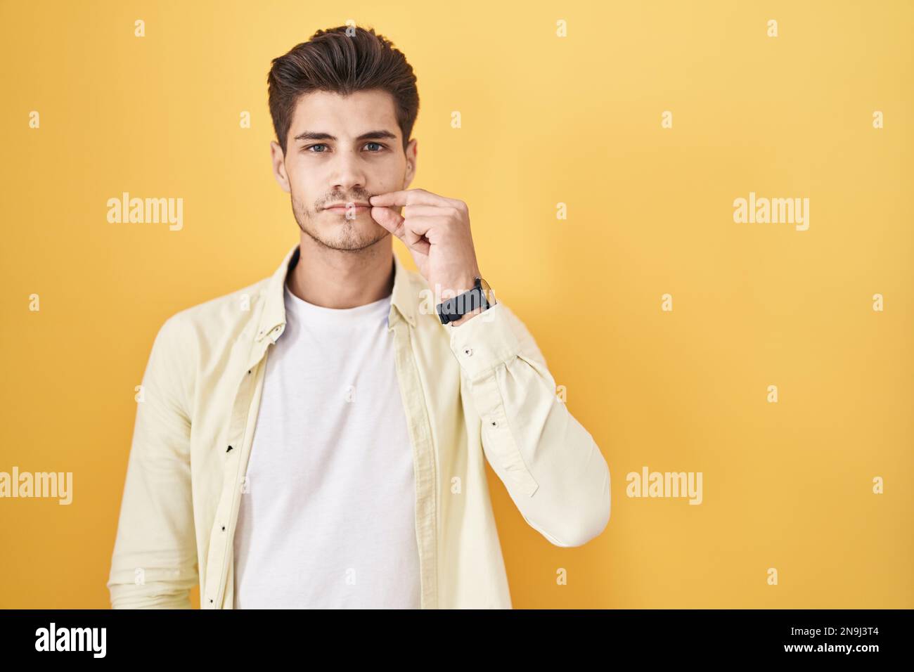 Young hispanic man standing over yellow background mouth and lips shut ...