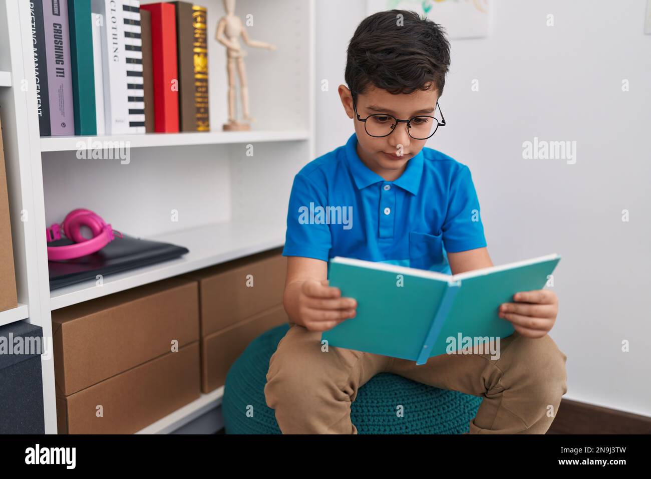 Adorable hispanic boy student reading book at library school Stock ...