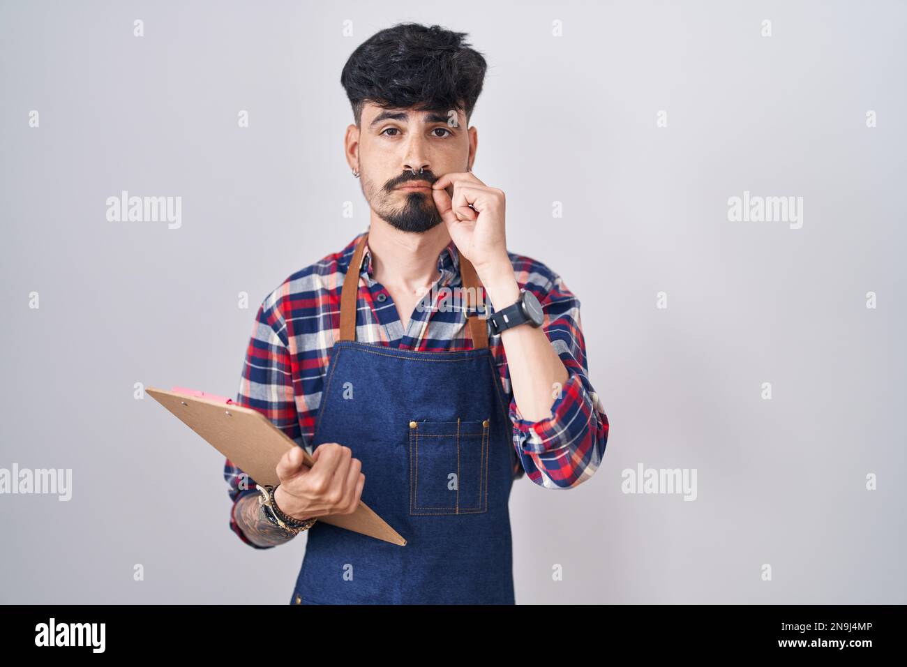 Young hispanic man with beard wearing waiter apron holding clipboard ...