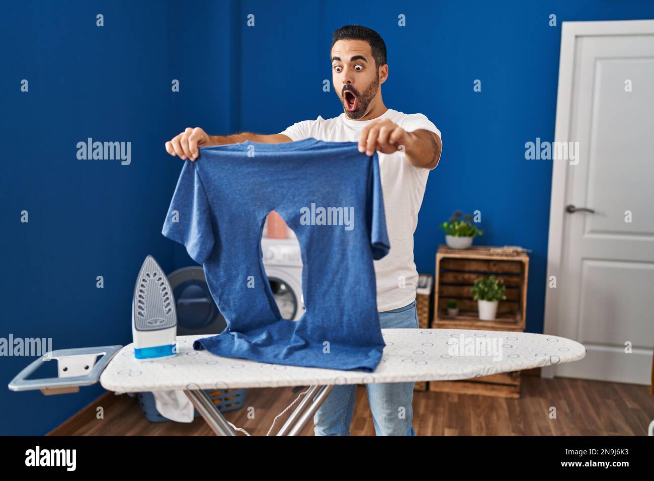Young hispanic man with beard ironing holding burned iron shirt at ...
