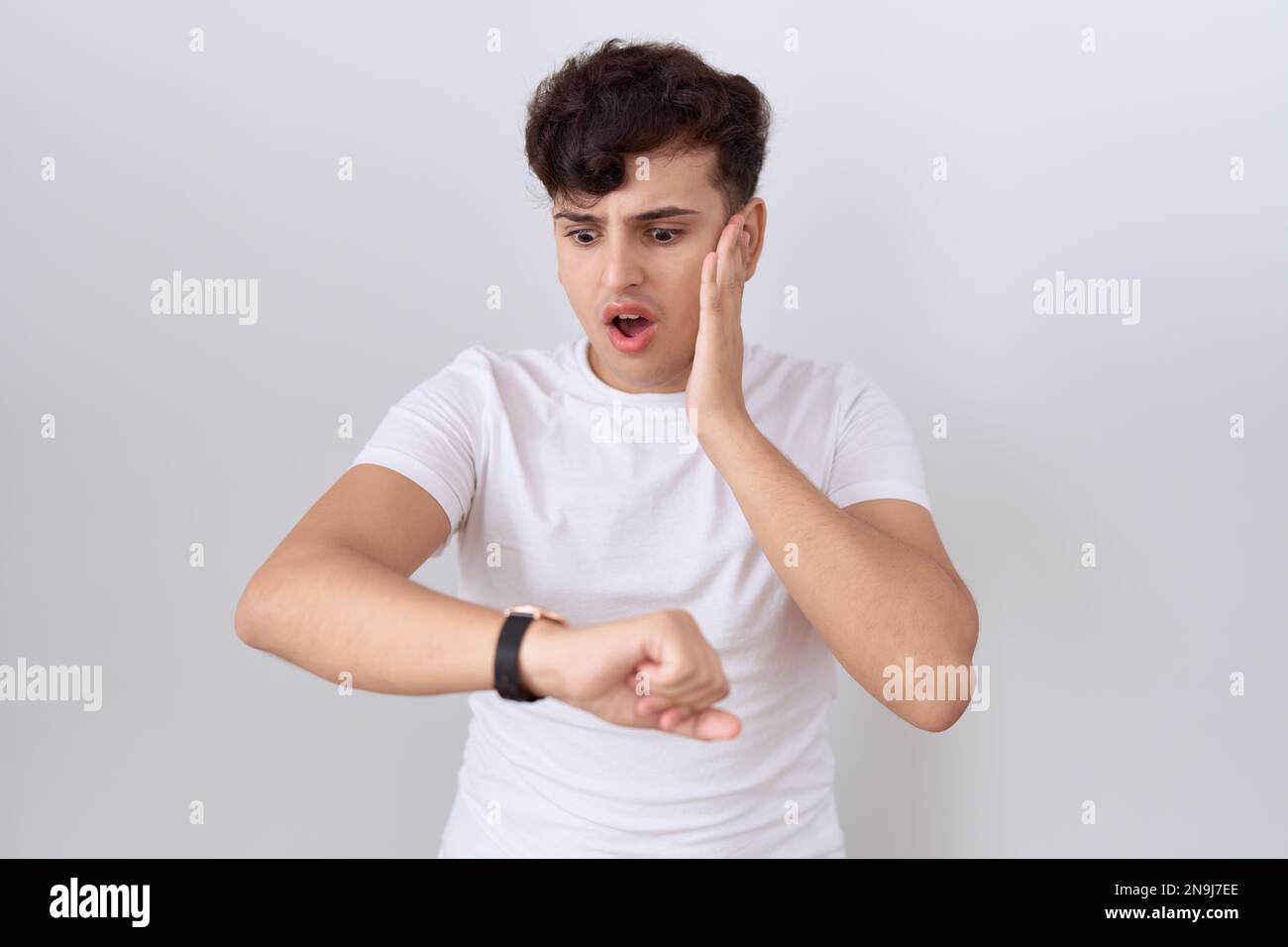 Young non binary man wearing casual white t shirt looking at the watch ...