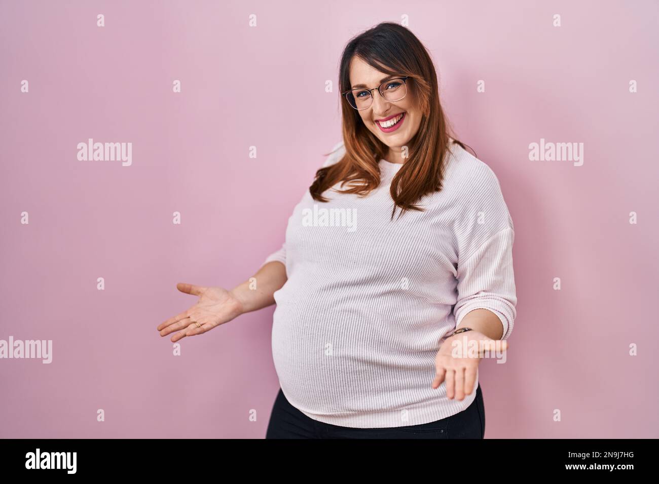 Pregnant woman standing over pink background smiling cheerful with open ...