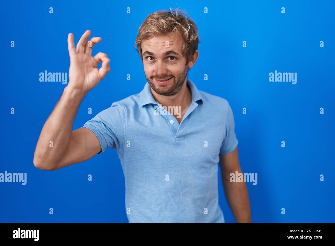 Caucasian man standing over blue background smiling positive doing ok ...