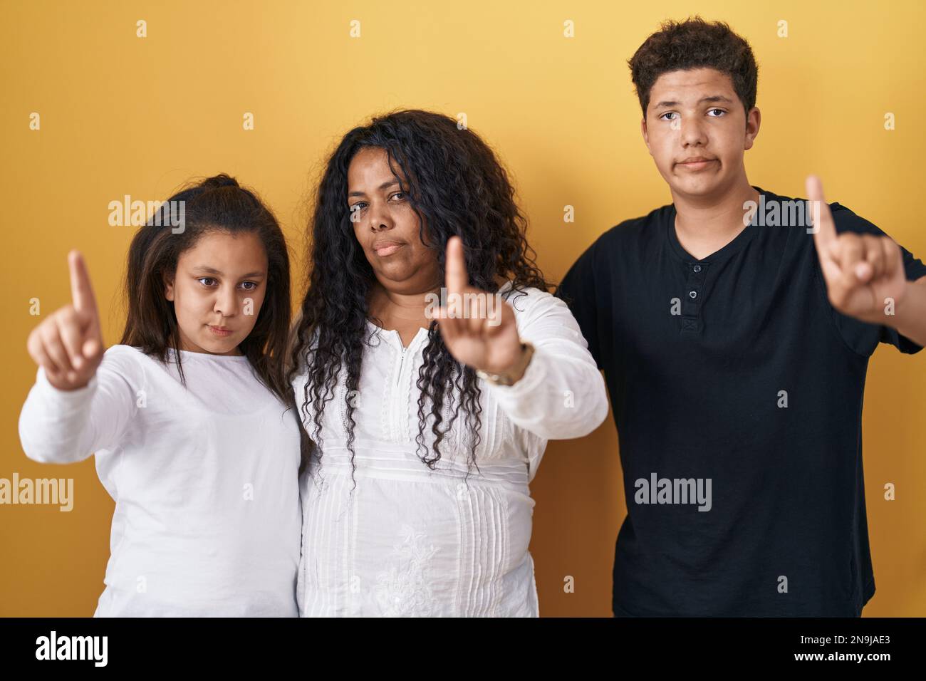 Family of mother, daughter and son standing over yellow background ...