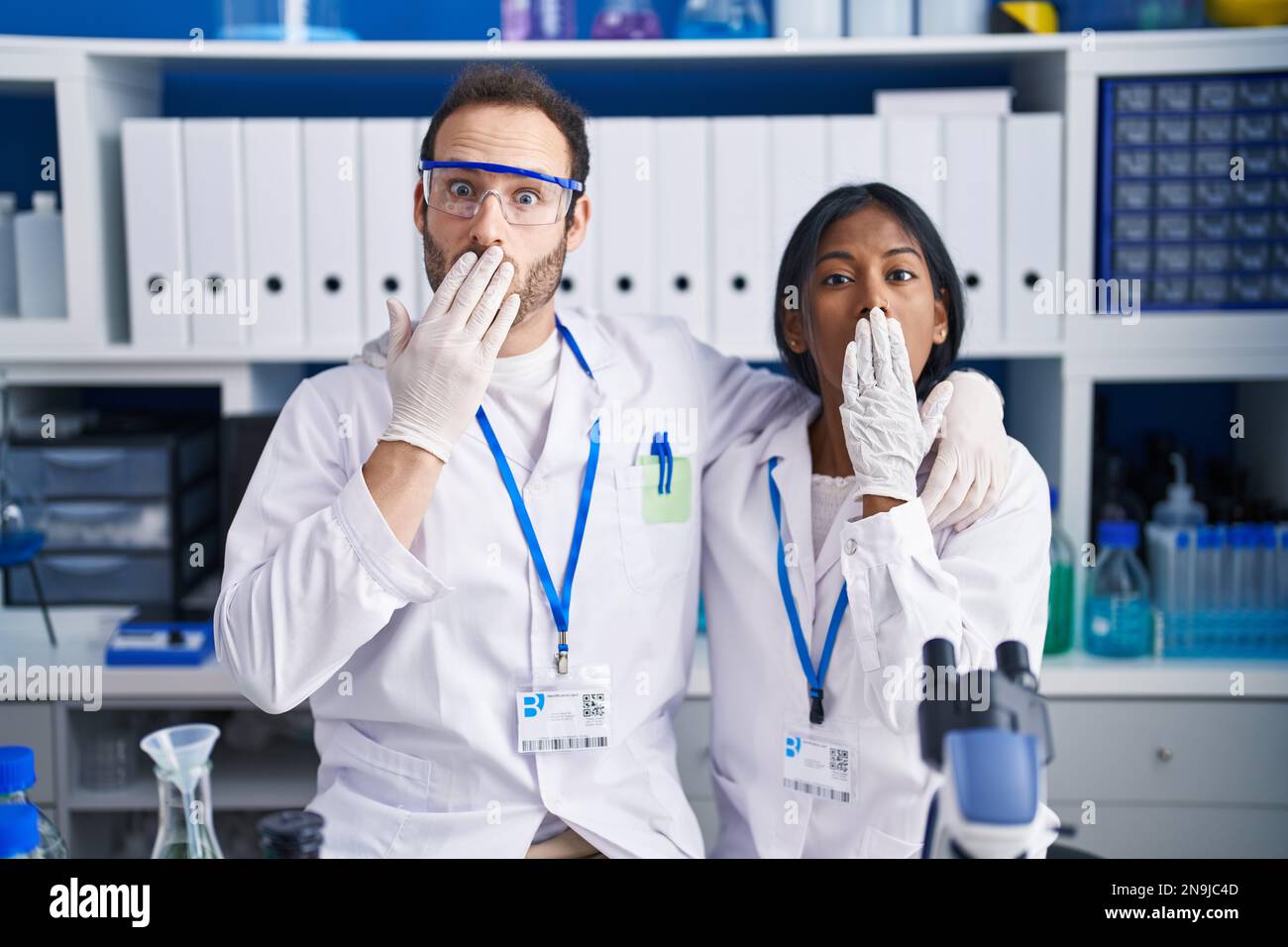 Interracial couple working at scientist laboratory covering mouth with ...