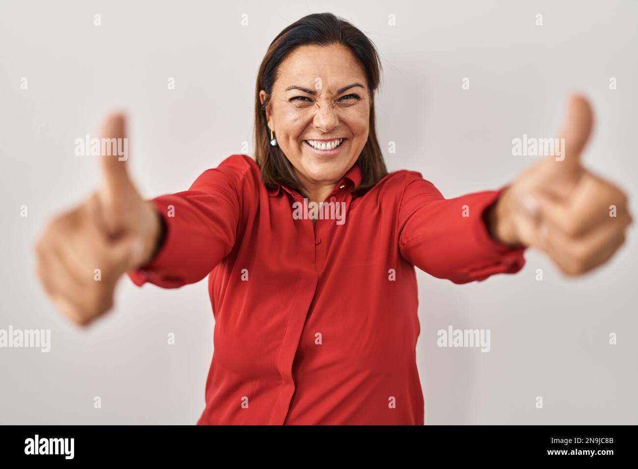 Hispanic mature woman standing over white background approving doing ...