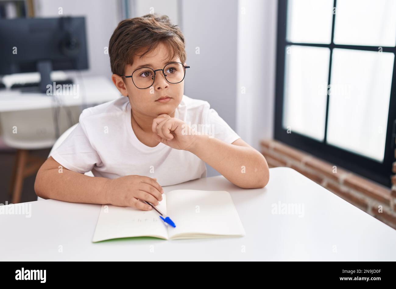 Adorable hispanic boy student reading book thinking at classroom Stock ...