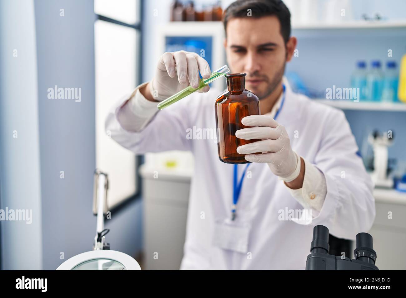 Young hispanic man scientist pouring liquid on bottle at laboratory ...