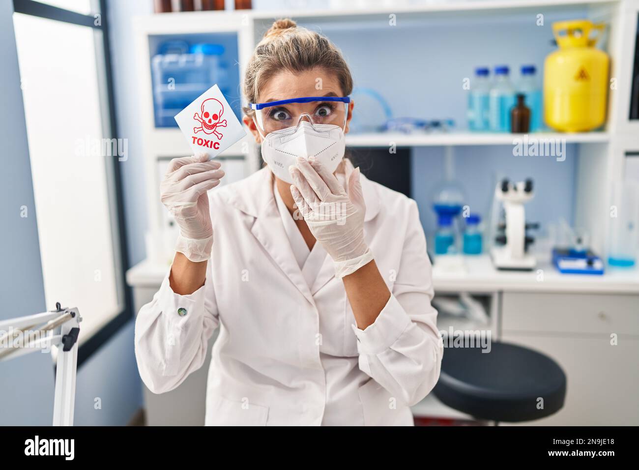 Young woman working at scientist laboratory holding toxic banner ...
