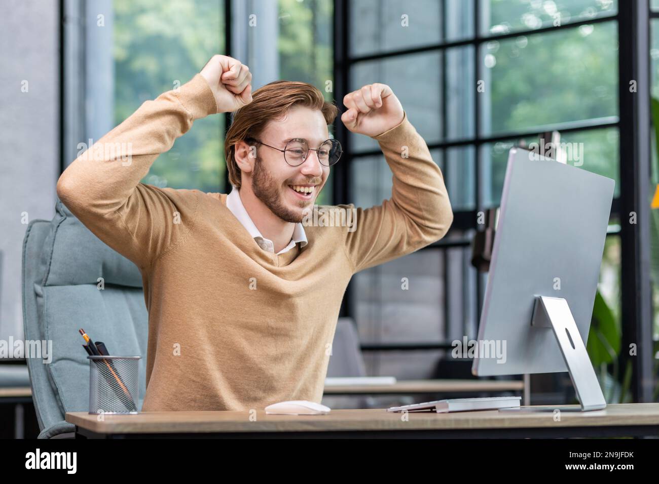 Smiling young male programmer, freelancer sits at the table, looks ...