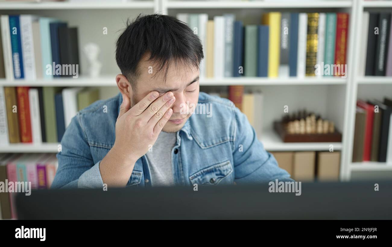 Young chinese man student using computer stressed at library university ...