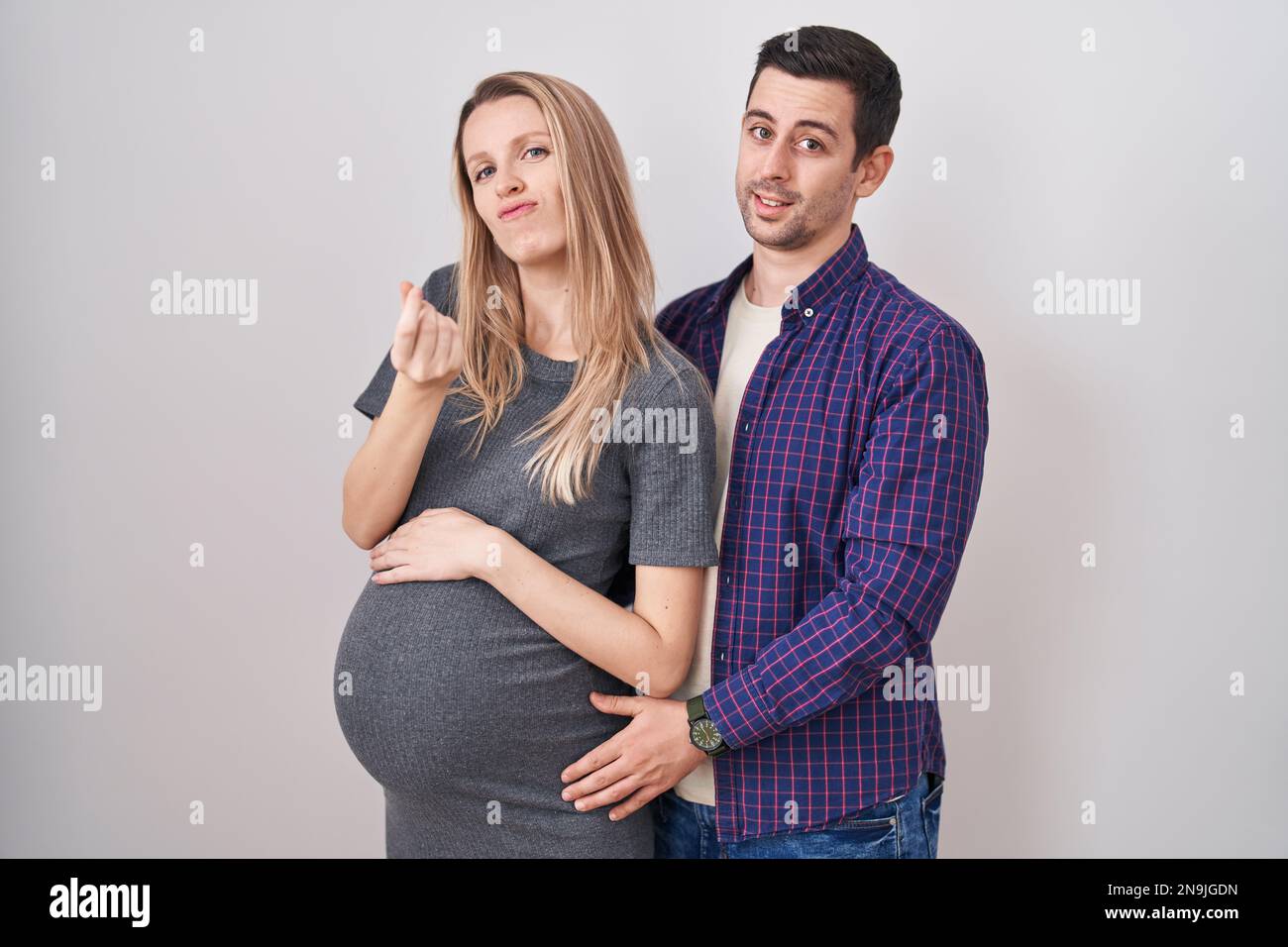Young couple expecting a baby standing over white background doing ...