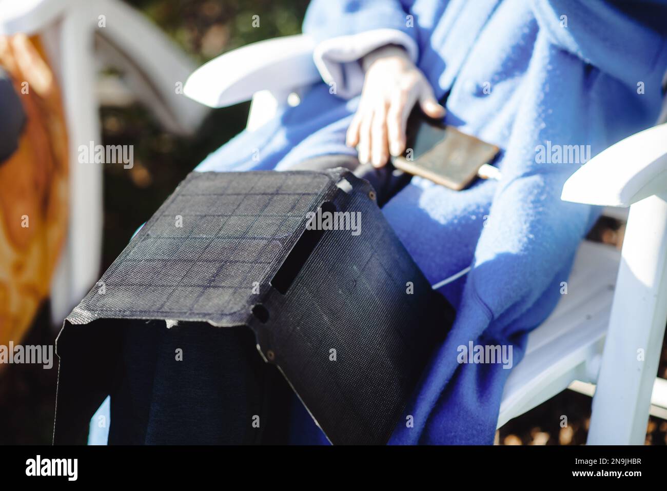 A portable solar battery rests on the legs of an unrecognizable woman ...