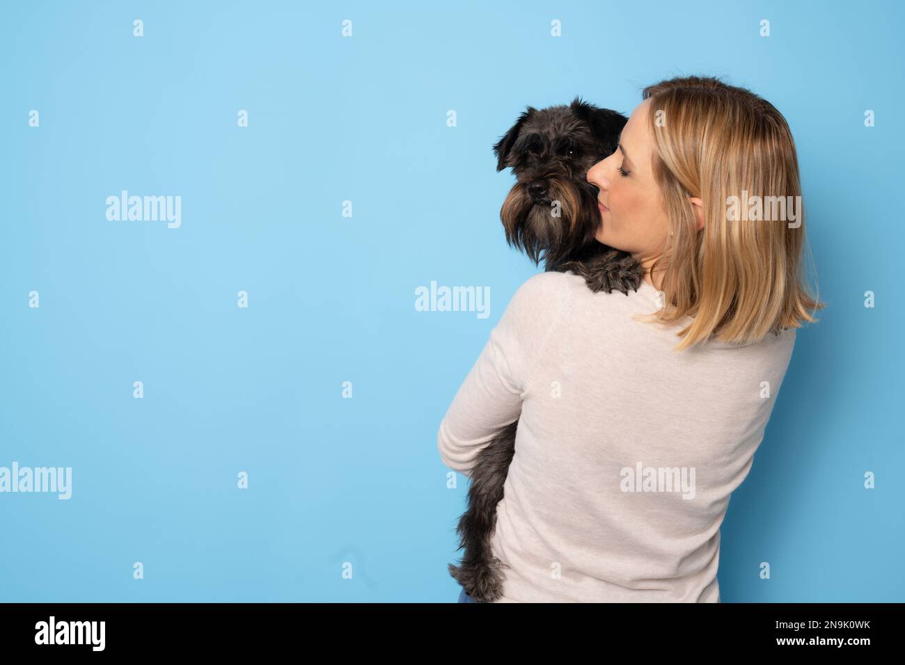 Cute young woman kisses and hugs her puppy Schnauzer dog. Love between ...