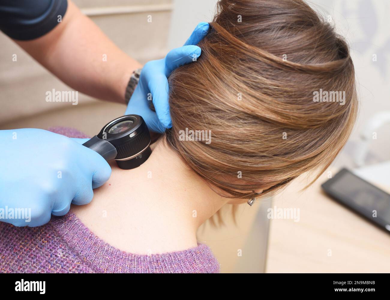 dermatologist examines a mole on the patient's neck using a special ...