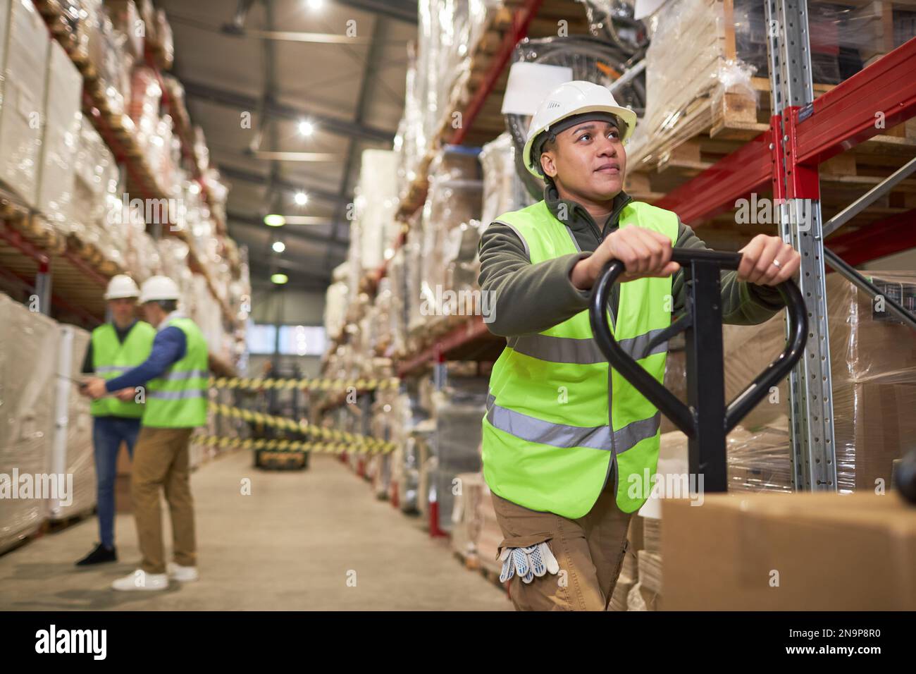 Portrait of female worker pushing cart carrier with boxes in storage ...