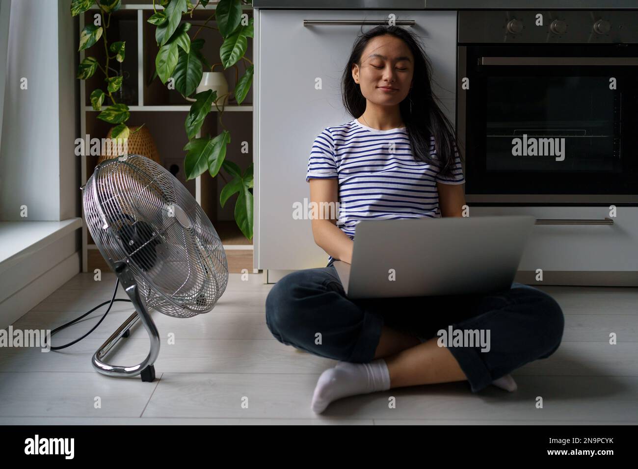 Contented Asian woman turn on floor ventilator fan while work with ...