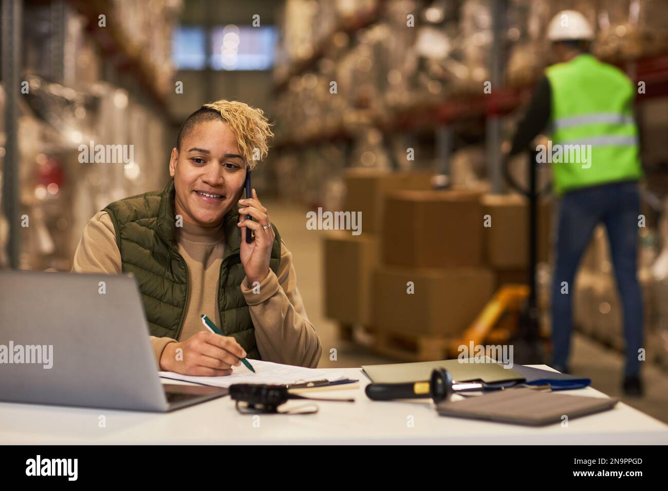 Portrait of smiling female worker using laptop in warehouse and calling ...