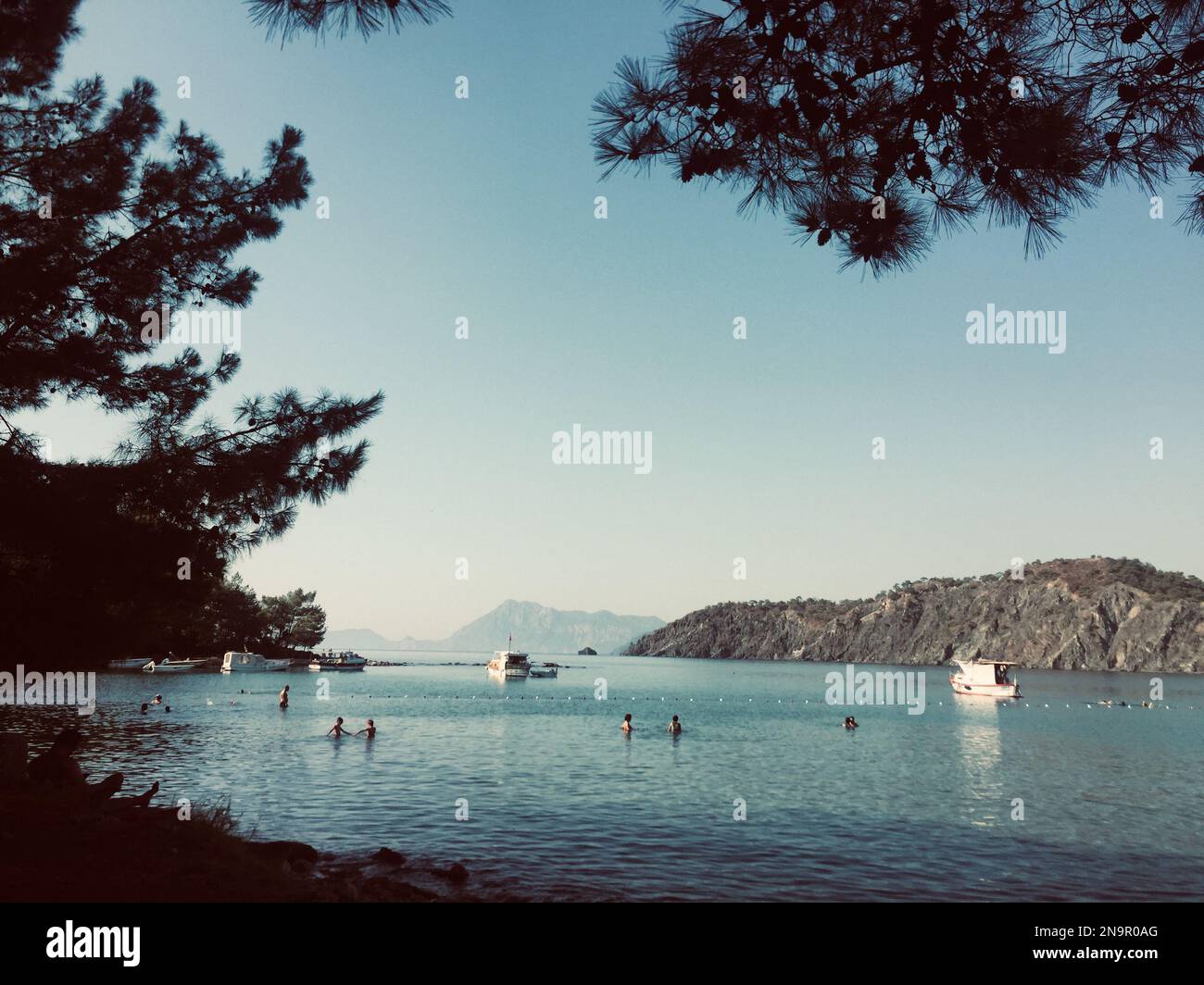 Beach view behind the trees. Swimming people, deserted island, boats ...