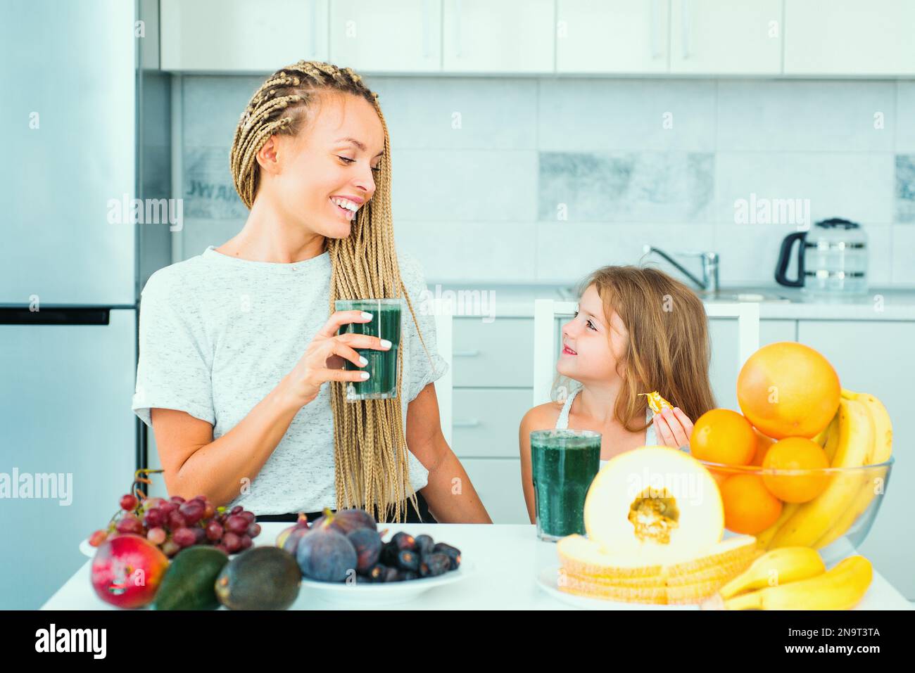 Mother and daughter drinking green smoothie in a white kitchen. Family ...